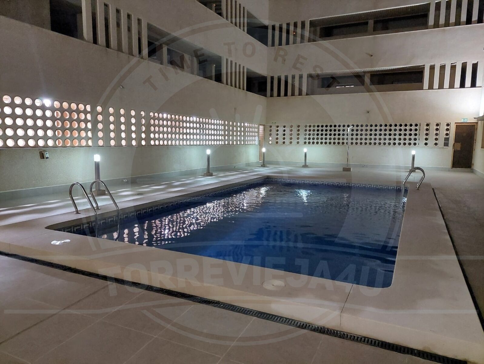 Piscina interior com piso ladrilhado e água com tonalidade azul.
