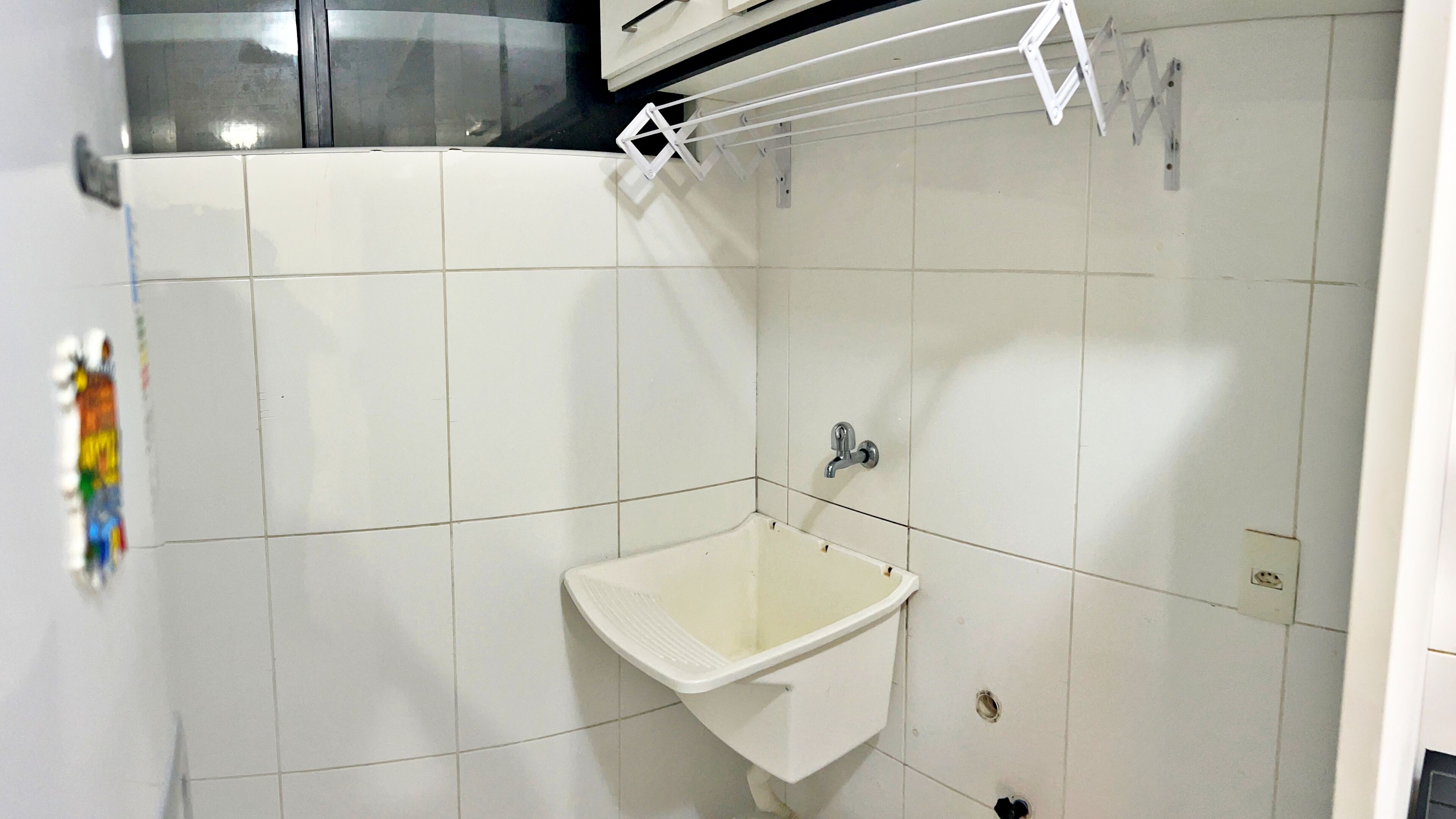 Casa de banho com azulejos brancos, uma pia branca e um porta-toalhas.