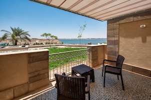 Varanda com vista para o mar, duas cadeiras de vime, uma mesa pequena e chão de azulejos.