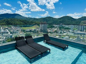 Piscina infinita no terraço com espreguiçadeiras e vista para a cidade.