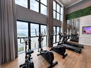 Uma academia com diversos equipamentos de exercício, amplas janelas e vista para o horizonte urbano.
