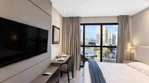 Quarto de hotel com cama, escrivaninha, televisão e janela com vista para a cidade.