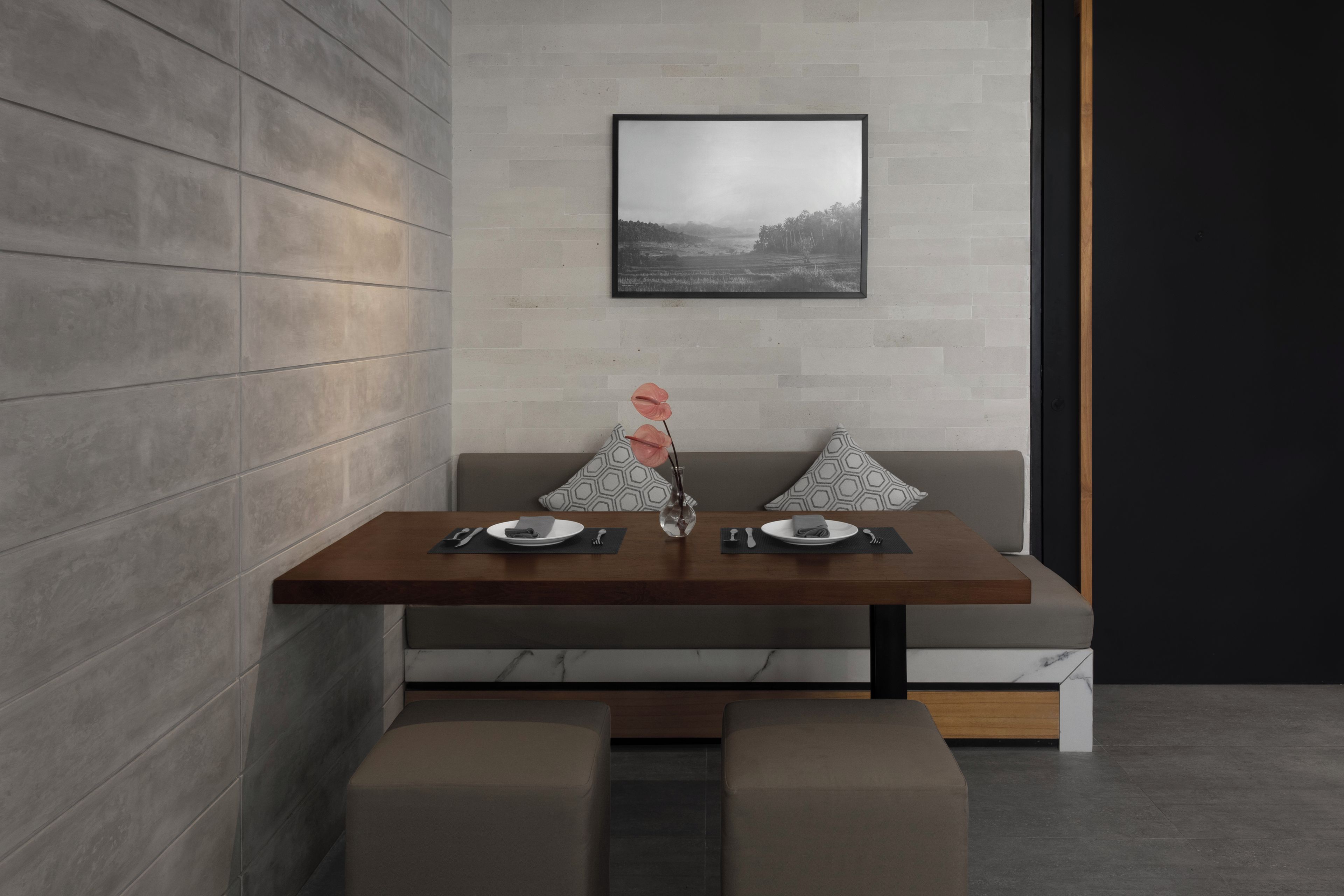 Uma área de jantar moderna com mesa de madeira posta para dois, um banco e um quadro na parede.