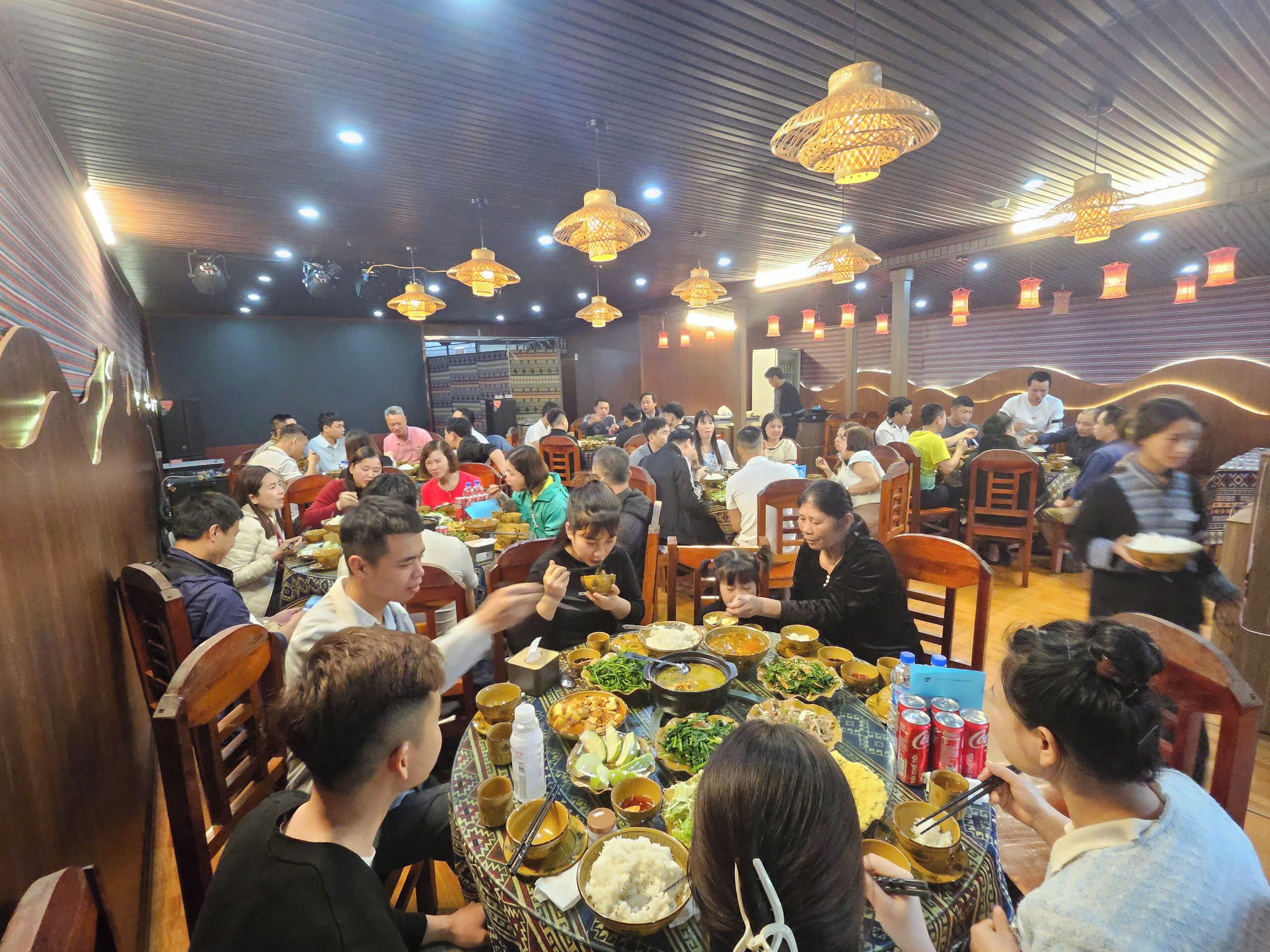 Restaurante movimentado com mesas redondas e luminárias pendentes.
