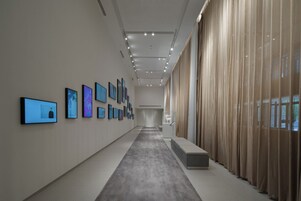 Uma galeria com um corredor comprido e estreito, um banco e uma série de obras de arte emolduradas nas paredes.