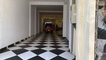 Um corredor com chão xadrez que leva a um aposento onde um carro vermelho está estacionado.