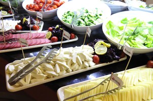 Buffet com diversas opções de comida, incluindo frios, queijos e saladas.