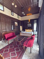 Quarto com cama de madeira, sofá vermelho, poltrona vermelha, mesa pequena e tapete estampado.