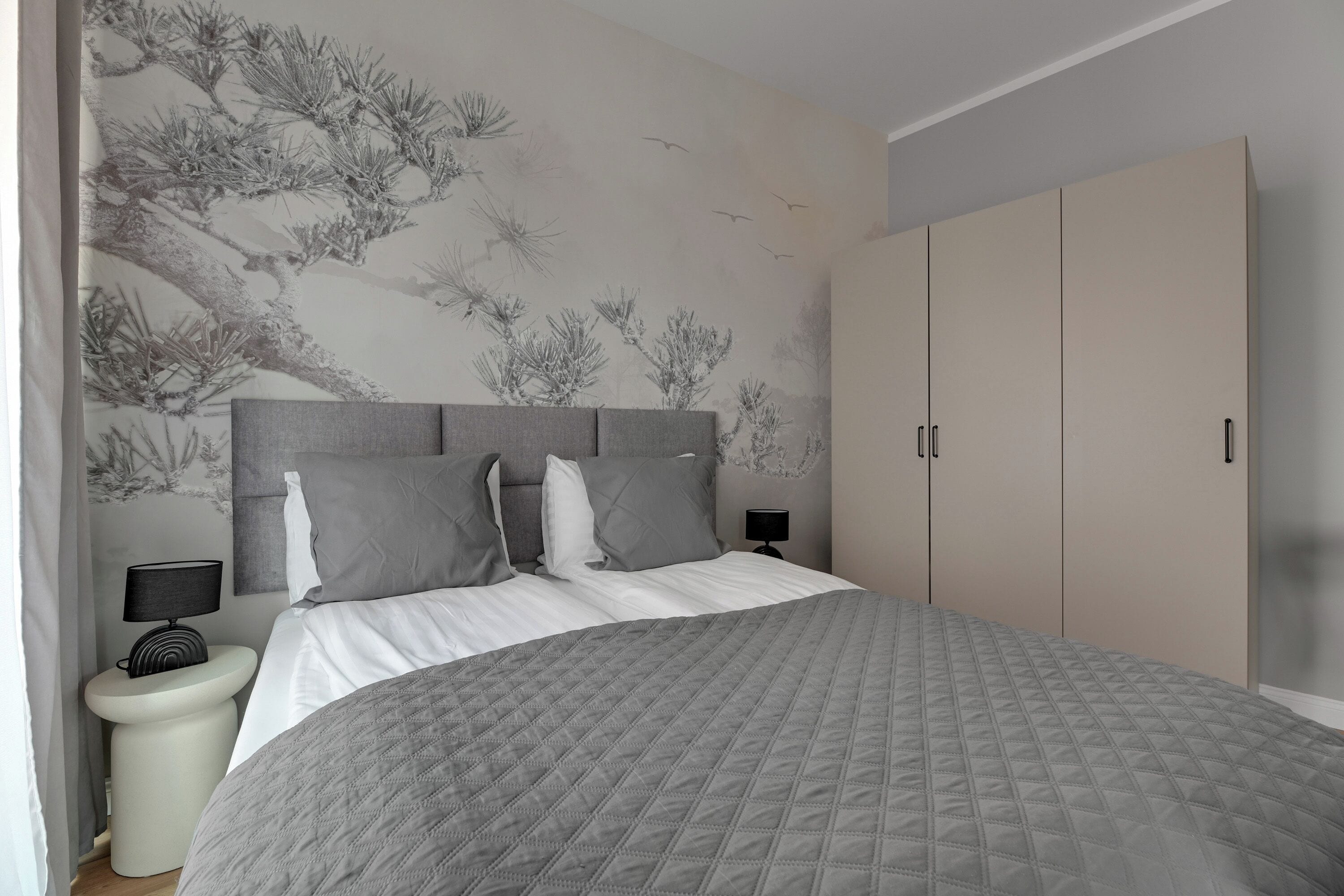 Quarto com uma cama grande, mesa de cabeceira com abajur, guarda-roupa e um mural na parede.