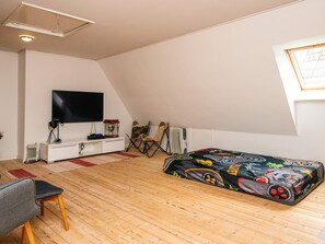 Quarto com teto inclinado, TV de tela plana na parede, cama com manta colorida, uma cadeira e um radiador.