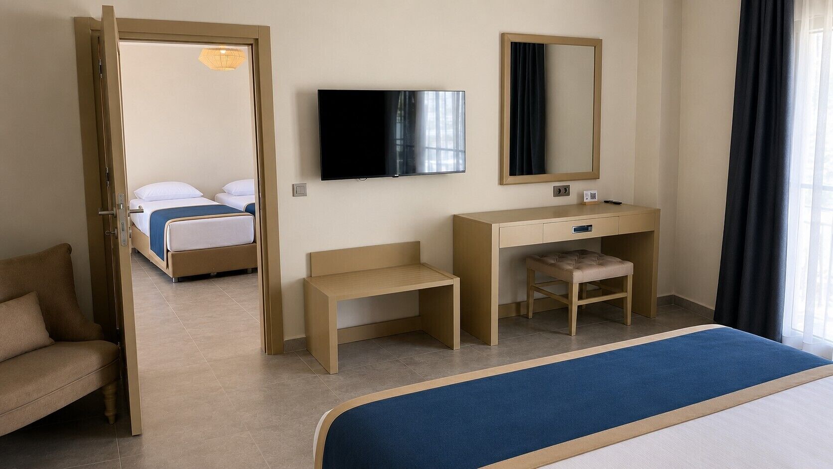 Quarto de hotel com cama, escrivaninha, cadeira, televisão e espelho.