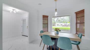 Uma sala de jantar com uma mesa de madeira, quatro cadeiras cor de verde-água e uma janela com persianas.