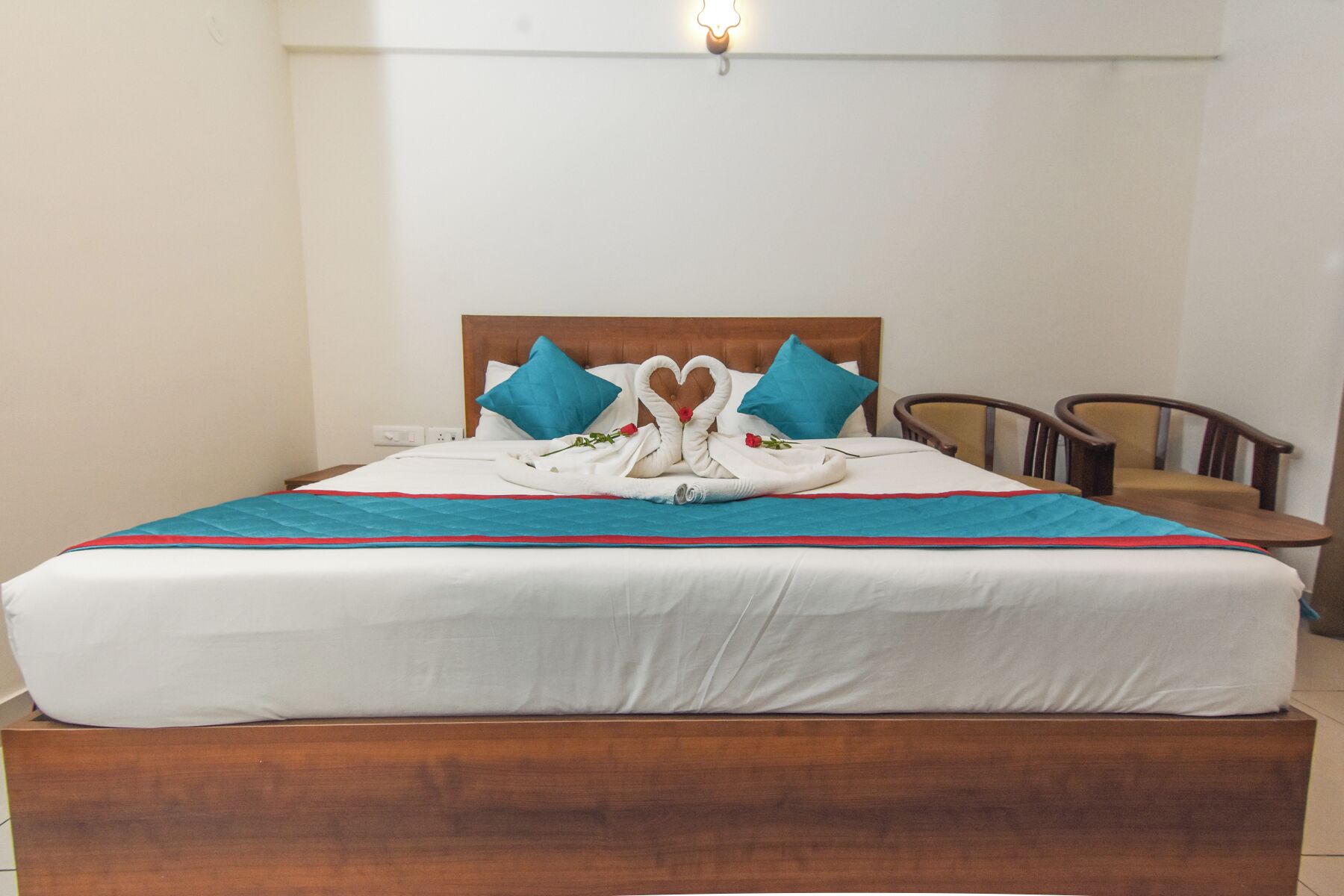 Cama bem arrumada com cabeceira de madeira, colcha azul-turquesa e vermelha, e dois travesseiros azuis.