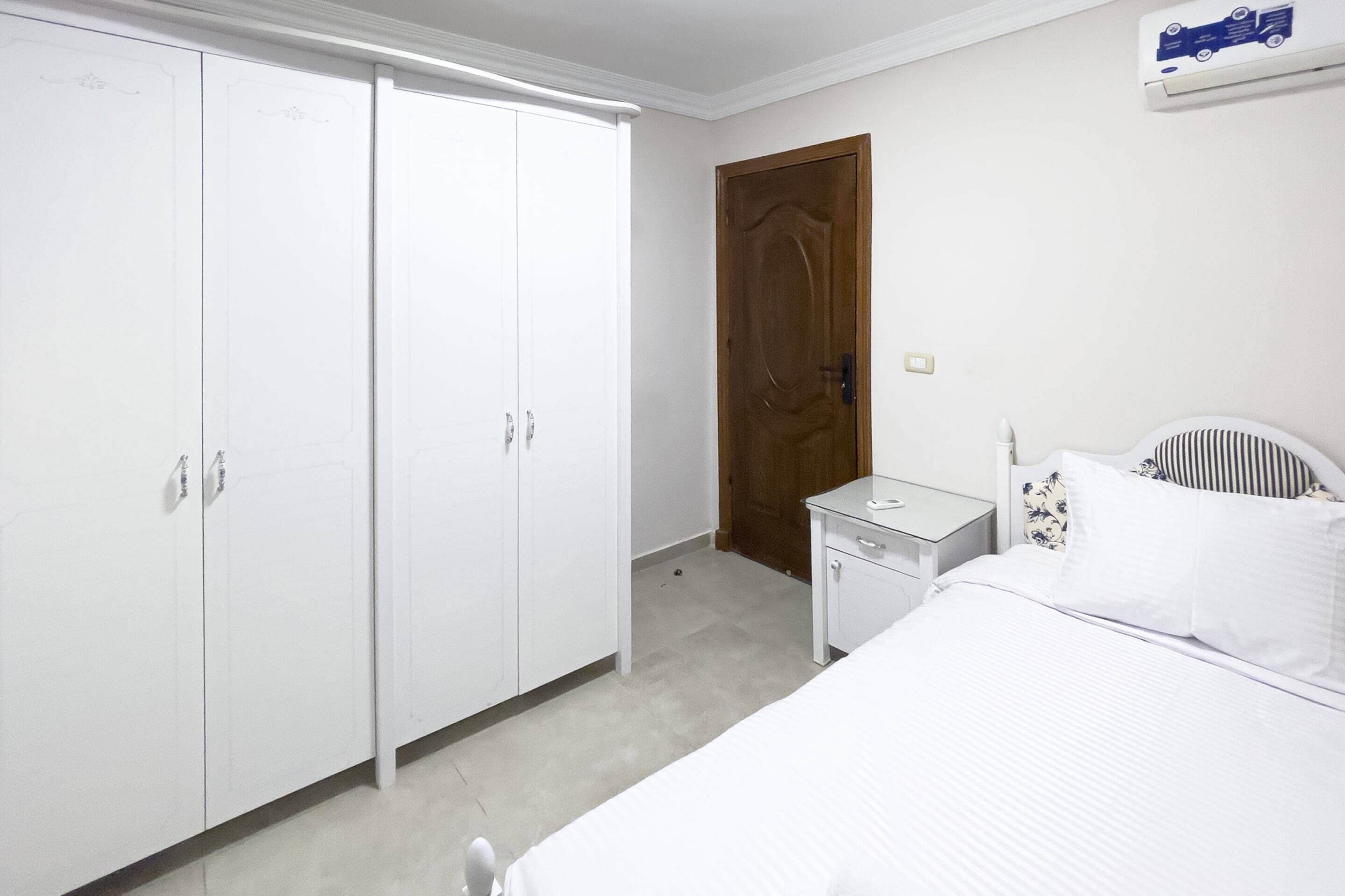 Quarto com cama, mesa de cabeceira, guarda-roupa e porta.