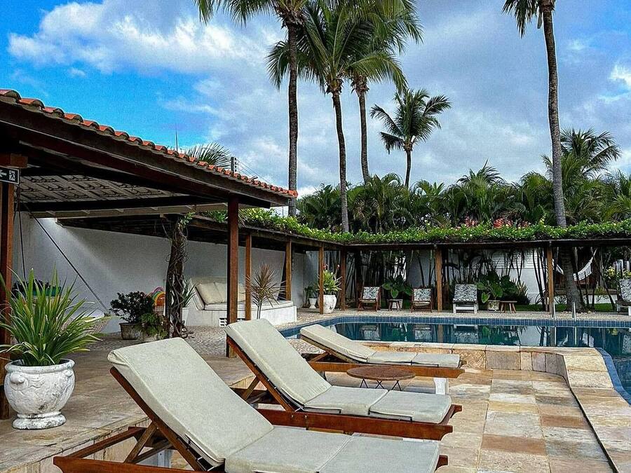 Uma área à beira da piscina com espreguiçadeiras, um deck revestido e palmeiras.