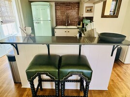 Uma cozinha com geladeira verde, pia, janela e um banquinho de bar.