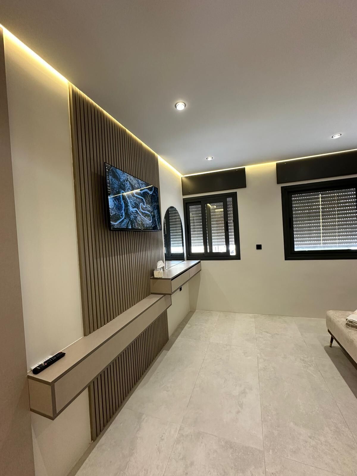 Uma sala de estar moderna com televisão de tela plana na parede, um banco embutido e uma janela com persianas.