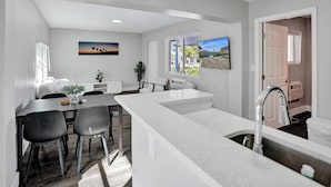 Cozinha moderna com uma ilha grande, sala de jantar com cadeiras e vista para o exterior através de uma janela.
