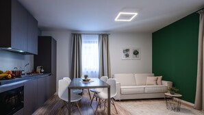 Cozinha moderna com mesa de jantar e cadeiras, sofá branco e uma parede verde de destaque.