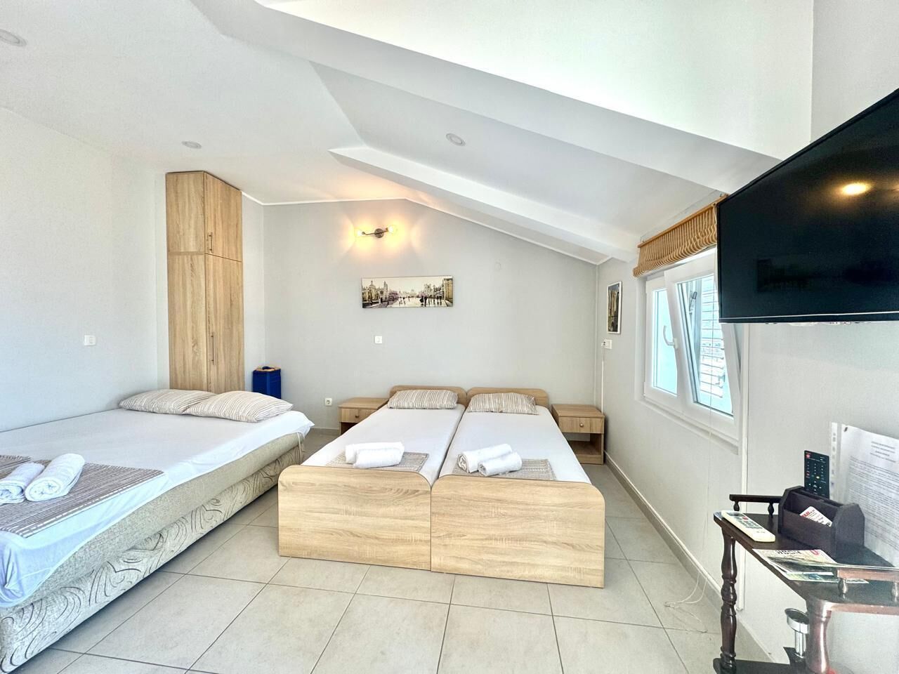 Quarto de hotel moderno com uma cama grande, uma cama menor e uma escrivaninha com televisão de tela plana.