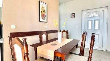 Uma área de refeições com mesa e cadeiras de madeira, um quadro na parede e uma porta ao fundo.