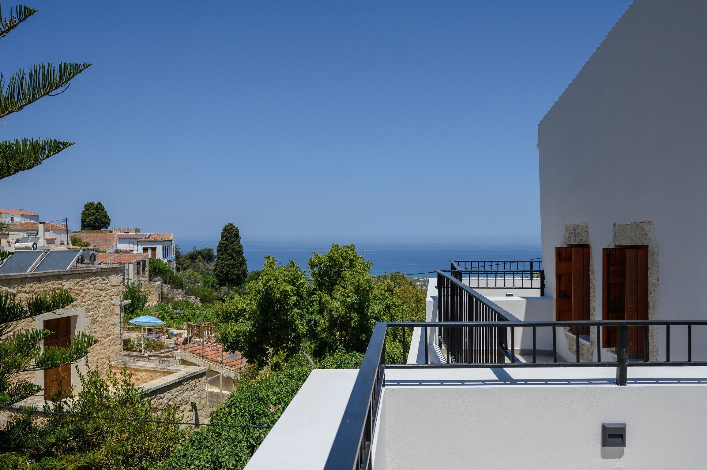 Uma área residencial costeira com um edifício branco, apresentando uma varanda com grade de metal, uma porta de madeira e uma pequena janela.