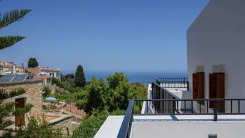 Uma área residencial costeira com um edifício branco, apresentando uma varanda com grade de metal, uma porta de madeira e uma pequena janela.