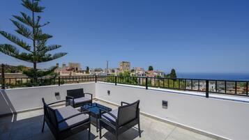 Terraço no terraço com mobiliário externo, vista para o mar e edifícios ao fundo.