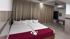Quarto de hotel com uma cama grande, cortinas bege, ventiladores de teto e uma pequena área de trabalho.