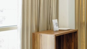 Quarto com mesa consola de madeira encostada à parede, janela com cortinas e um letreiro sobre a mesa.