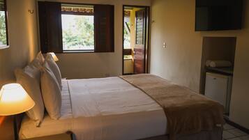 Cama bem arrumada com edredom branco e marrom, luminária de cabeceira e controle remoto em uma mesinha de cabeceira.