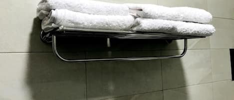 Um porta-toalhas de metal com toalhas brancas dobradas em frente a uma parede revestida de azulejos.
