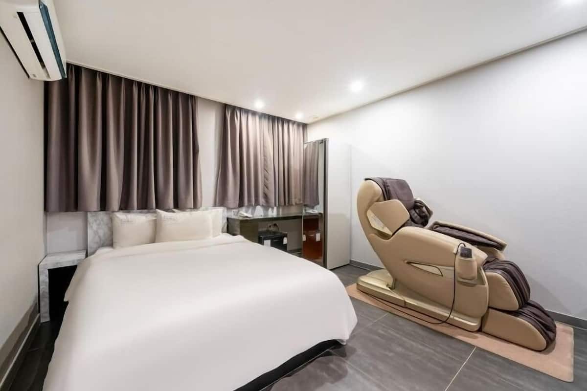Quarto de hotel moderno com uma cama grande, uma cadeira de massagem e um minibar.
