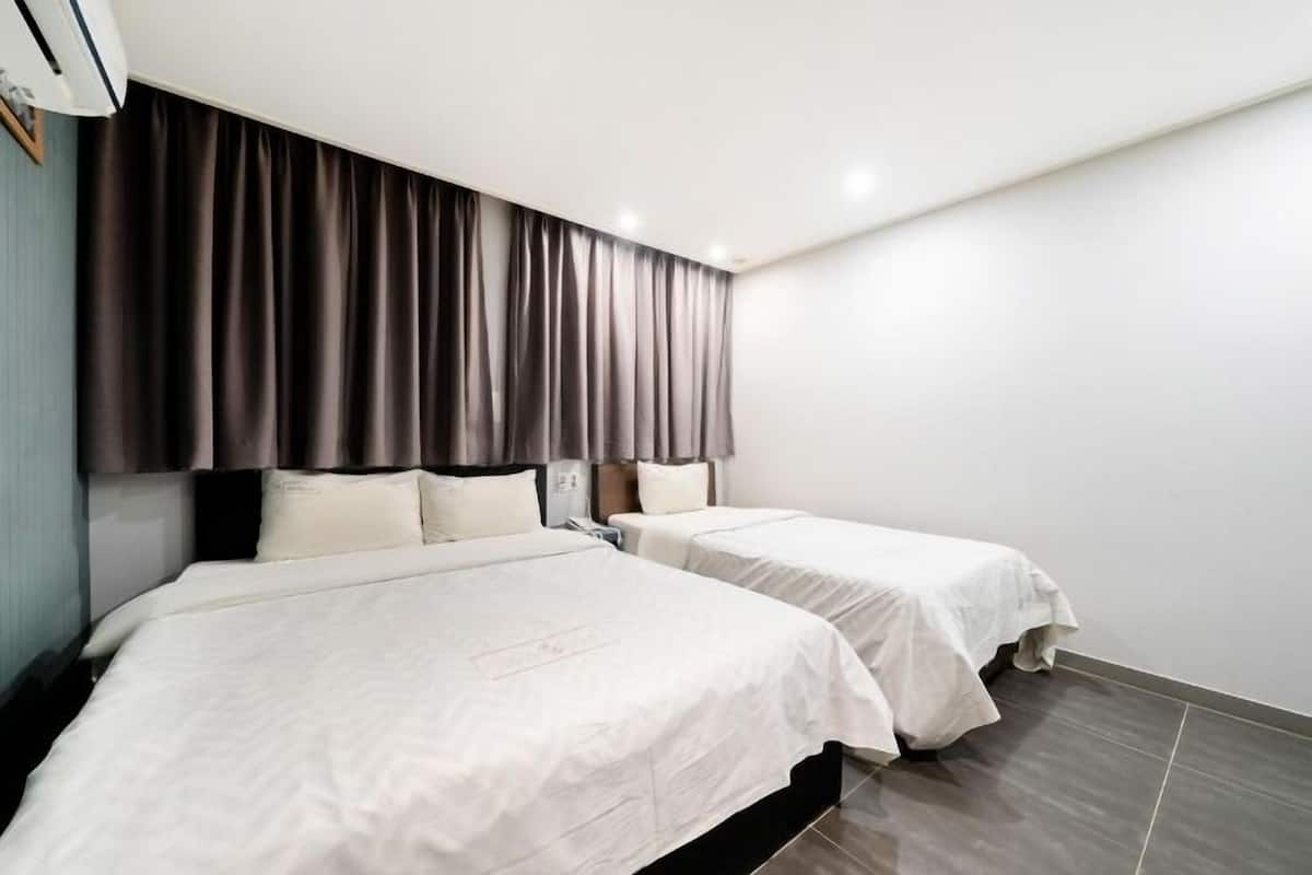 Quarto de hotel moderno com duas camas, uma janela grande com cortinas e um ar condicionado integrado.
