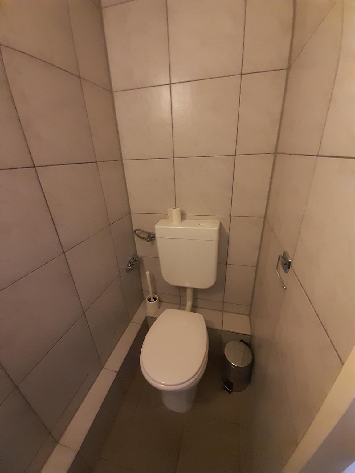 Um banheiro pequeno revestido com azulejos, com vaso sanitário, bidê e lixeira.