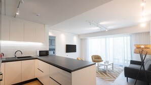 Cozinha moderna com armários brancos, bancada preta e micro-ondas embutido. Possui área de jantar com mesa e cadeiras, além de uma grande janela com cortinas.