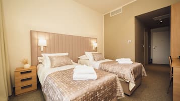 Quarto de hotel com duas camas, uma mesinha de cabeceira de madeira e uma escrivaninha.
