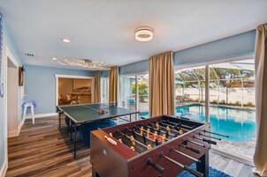 Um quarto com mesa de pebolim, mesa de bilhar e área de estar com sofá e cadeiras.