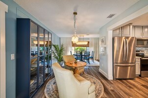 Cozinha moderna com eletrodomésticos de aço inoxidável, sala de jantar com mesa e cadeiras redondas, e uma grande janela que oferece luz natural.