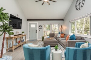 Uma sala de estar espaçosa com um amplo sofá modular, duas poltronas, uma mesa de centro e uma TV fixada na parede. Há uma janela grande que oferece vista para o exterior.