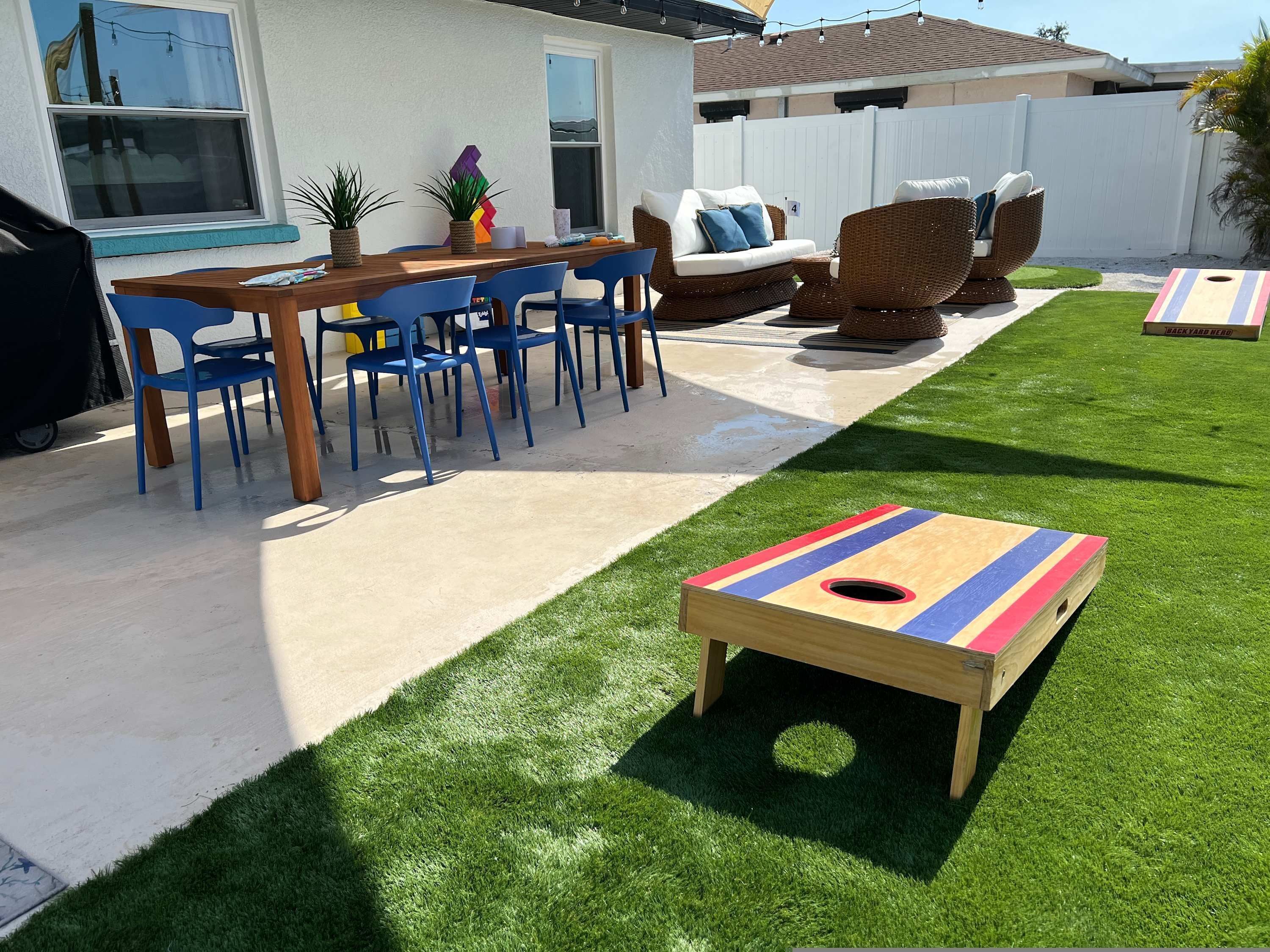 Um quintal com mesa e cadeiras de madeira, um sofá estofado e uma mesa de jogos de madeira colorida.