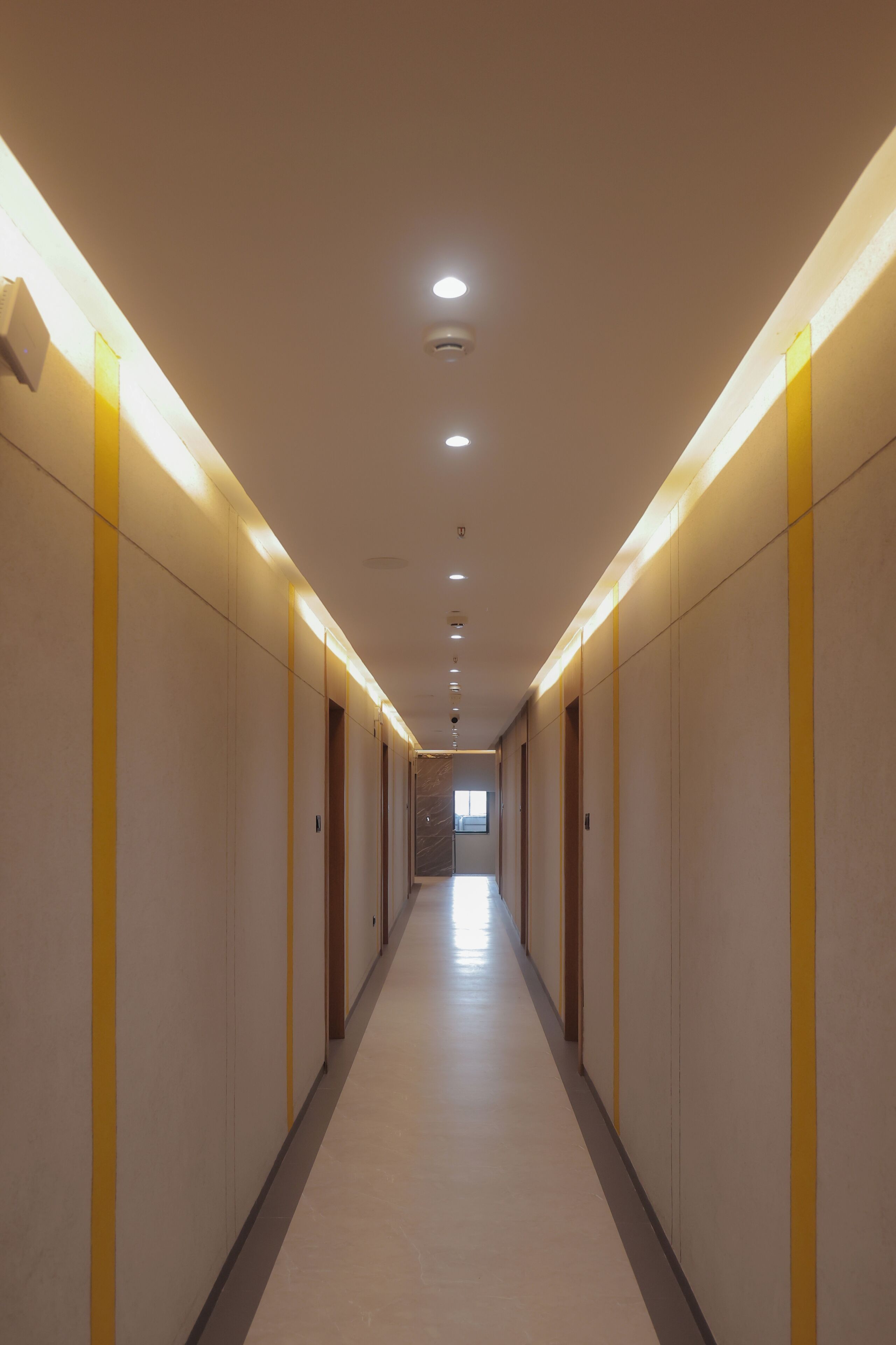 Um corredor longo e bem iluminado, com portas em ambos os lados, que dá acesso a quartos.