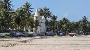 Uma área à beira-mar com uma igreja branca, palmeiras e uma praia de areia.