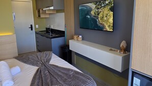 Quarto de hotel moderno com uma cama grande, televisão de tela plana na parede, pequena cozinha e uma mesa de jantar.