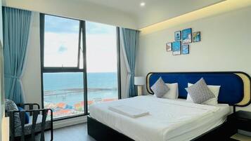 Quarto de hotel moderno com uma cama grande, vista para o mar e para a paisagem urbana.