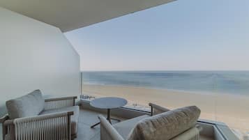 Uma varanda com vista para a praia, equipada com duas cadeiras e uma mesa pequena.