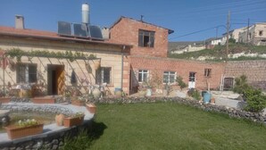 Uma propriedade residencial com casa de tijolos, muro de pedra e um pequeno jardim com plantas em vasos.