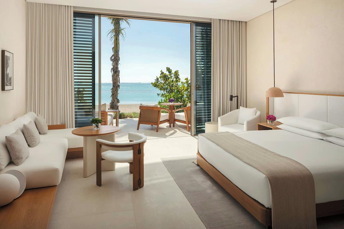Quarto de hotel com cama, sofá, mesa de jantar e vista para o mar.