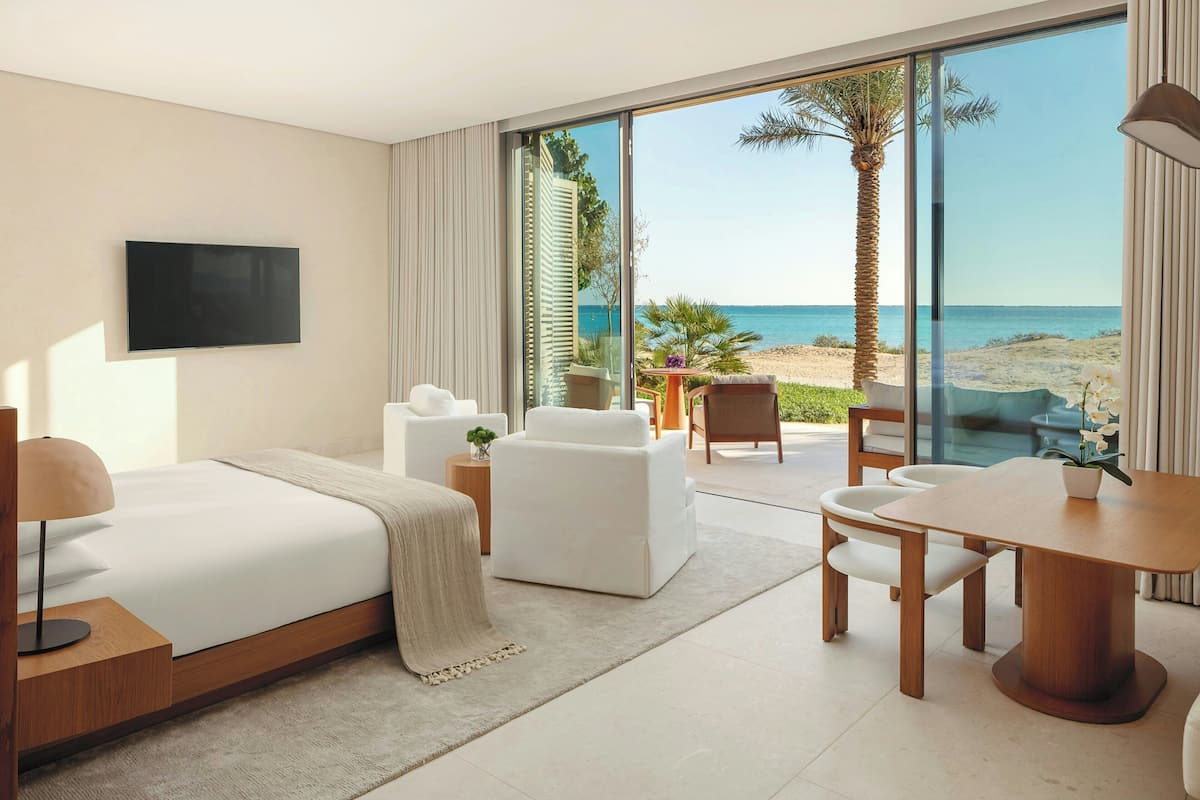 Quarto de hotel moderno com uma cama grande, uma escrivaninha e vista para a praia.