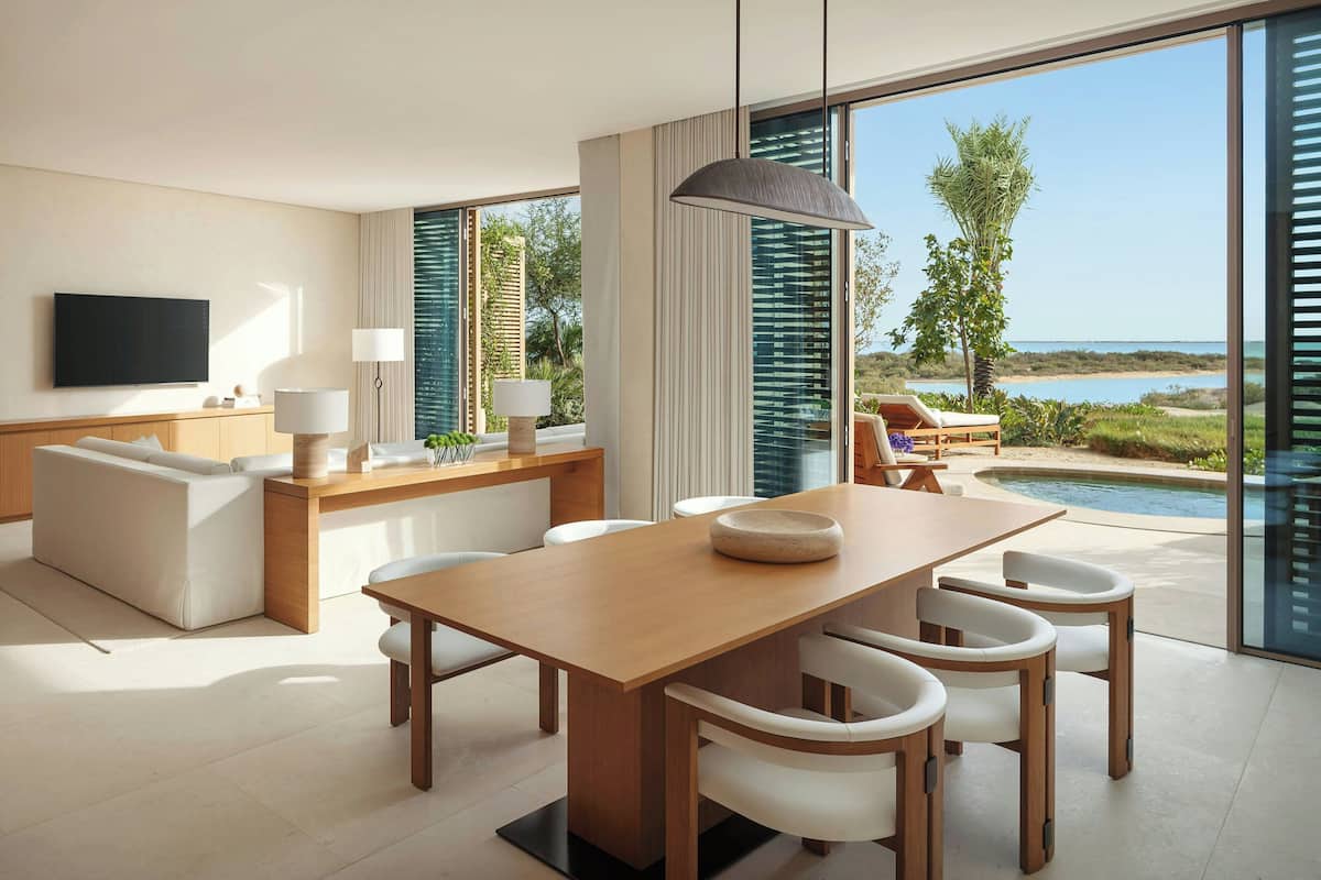 Quarto de hotel moderno com área de refeições, televisão e vista para a praia.